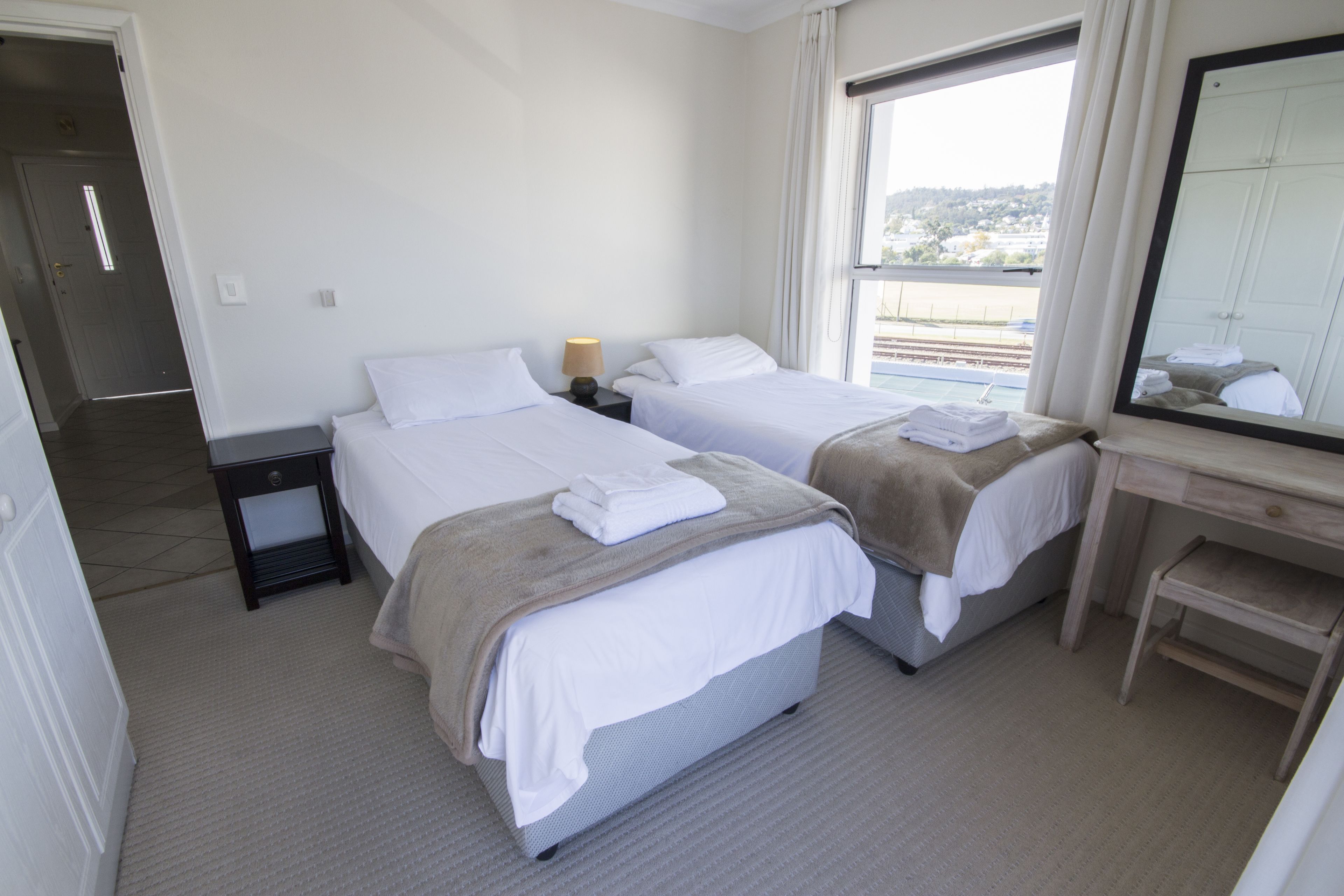 Quarto de hotel com duas camas, uma escrivaninha e uma janela grande com vista.