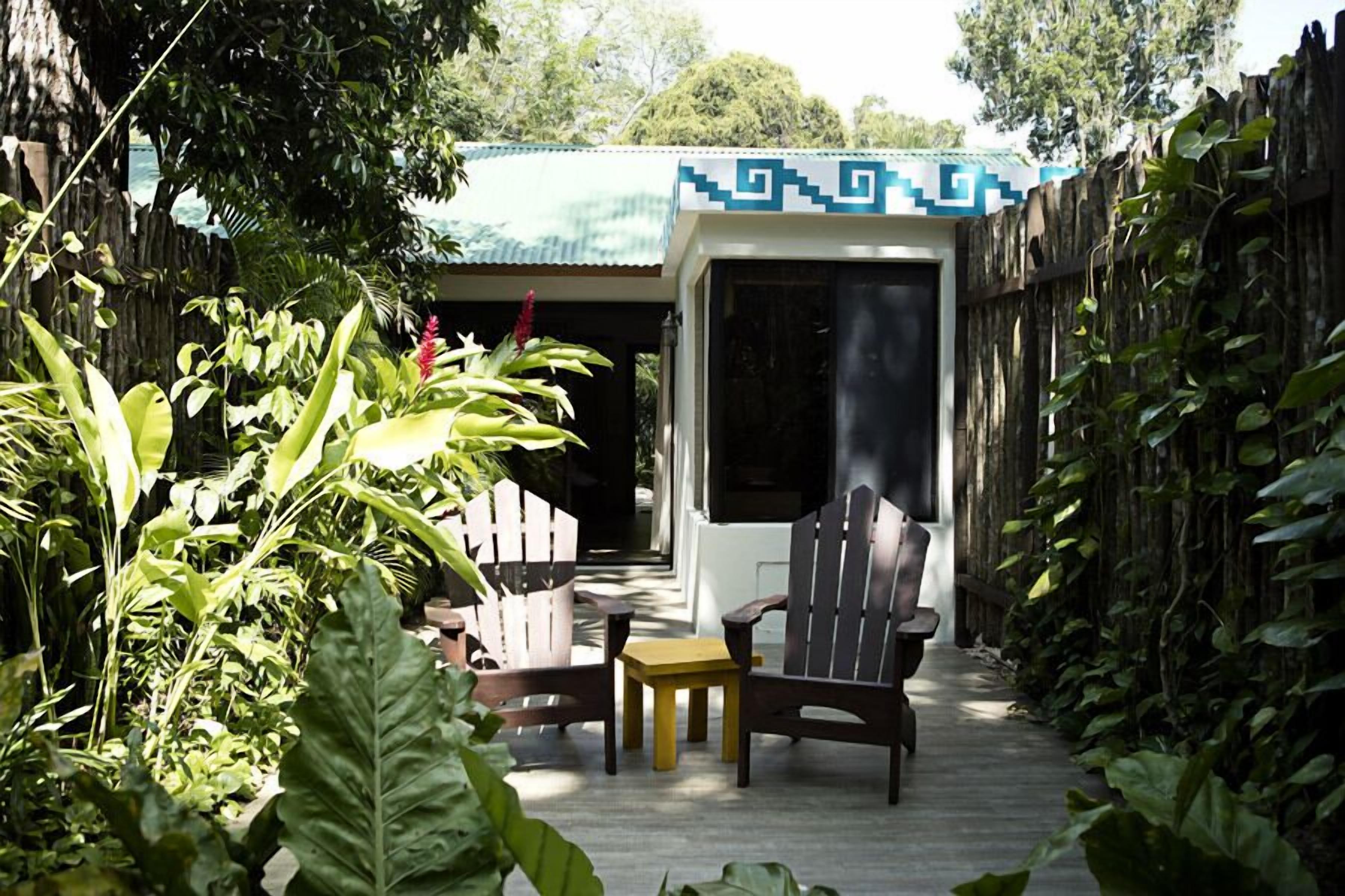 Um deck de madeira com uma cadeira e mesa, cercado por vegetação exuberante.
