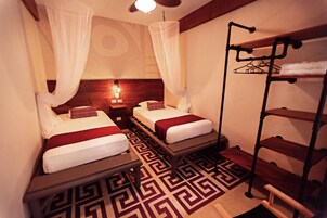 Quarto de hotel com duas camas, mesa de cabeceira, cabideiro e piso estampado.
