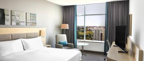 Quarto de hotel com cama, secretária, cadeira, televisão e janela com vista para a cidade.