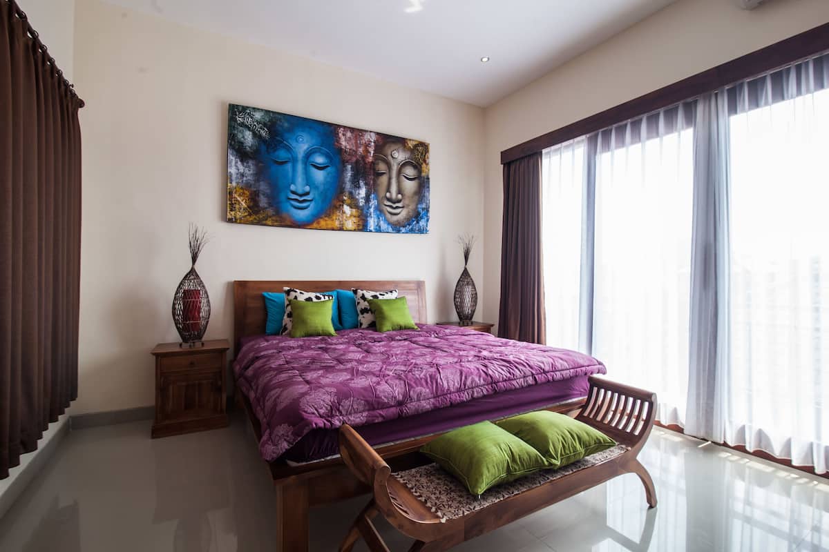 Quarto com uma cama grande, um banco de madeira, uma mesa de cabeceira e um quadro na parede.