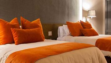 Quarto de hotel com duas camas, cada uma com roupa de cama e almofadas laranja.