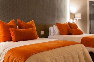 Quarto de hotel com duas camas, cada uma com roupa de cama e almofadas laranja.