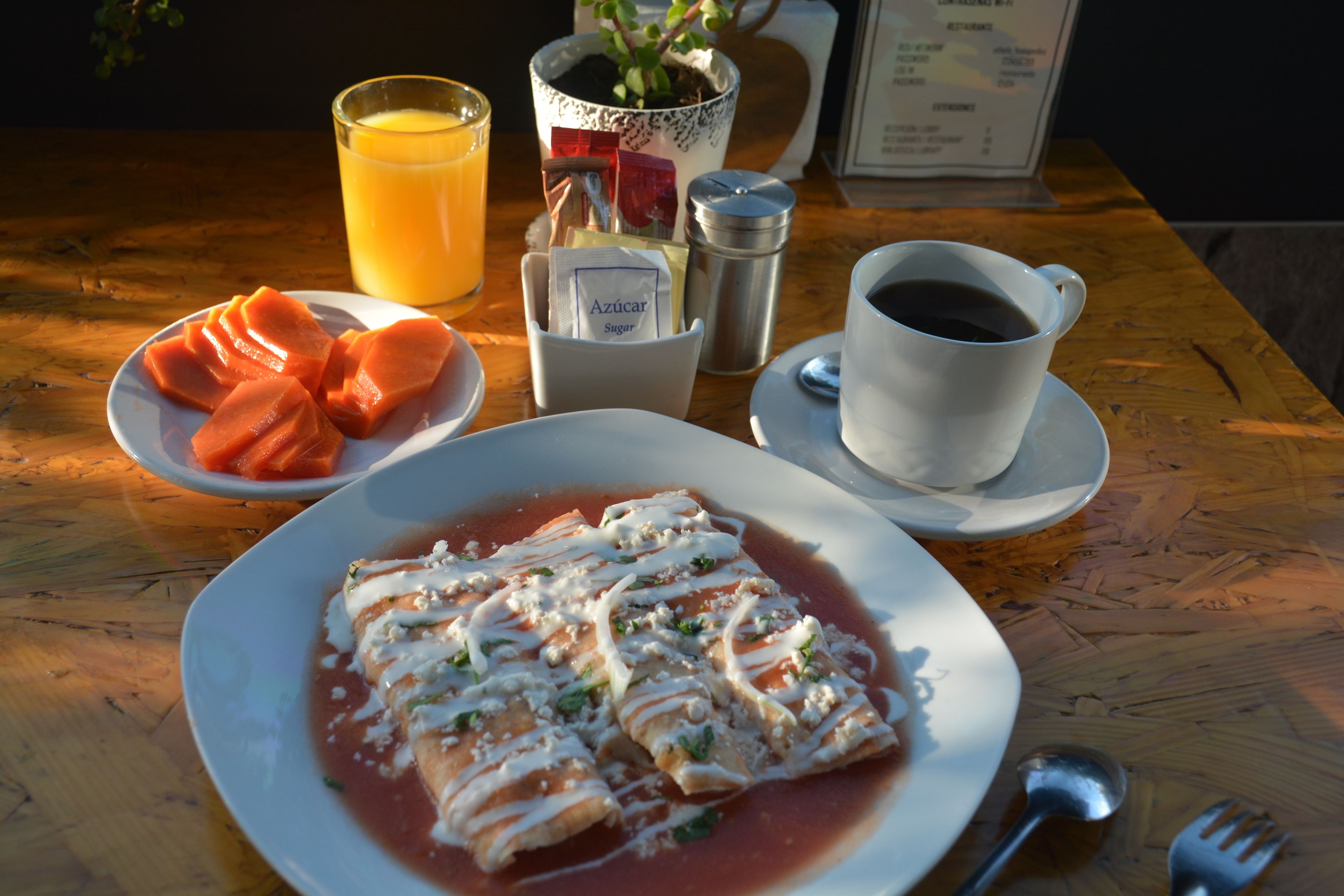 Uma mesa com um prato de enchiladas, um copo de suco de laranja e uma xícara de café.