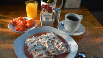 Uma mesa com um prato de enchiladas, um copo de suco de laranja e uma xícara de café.