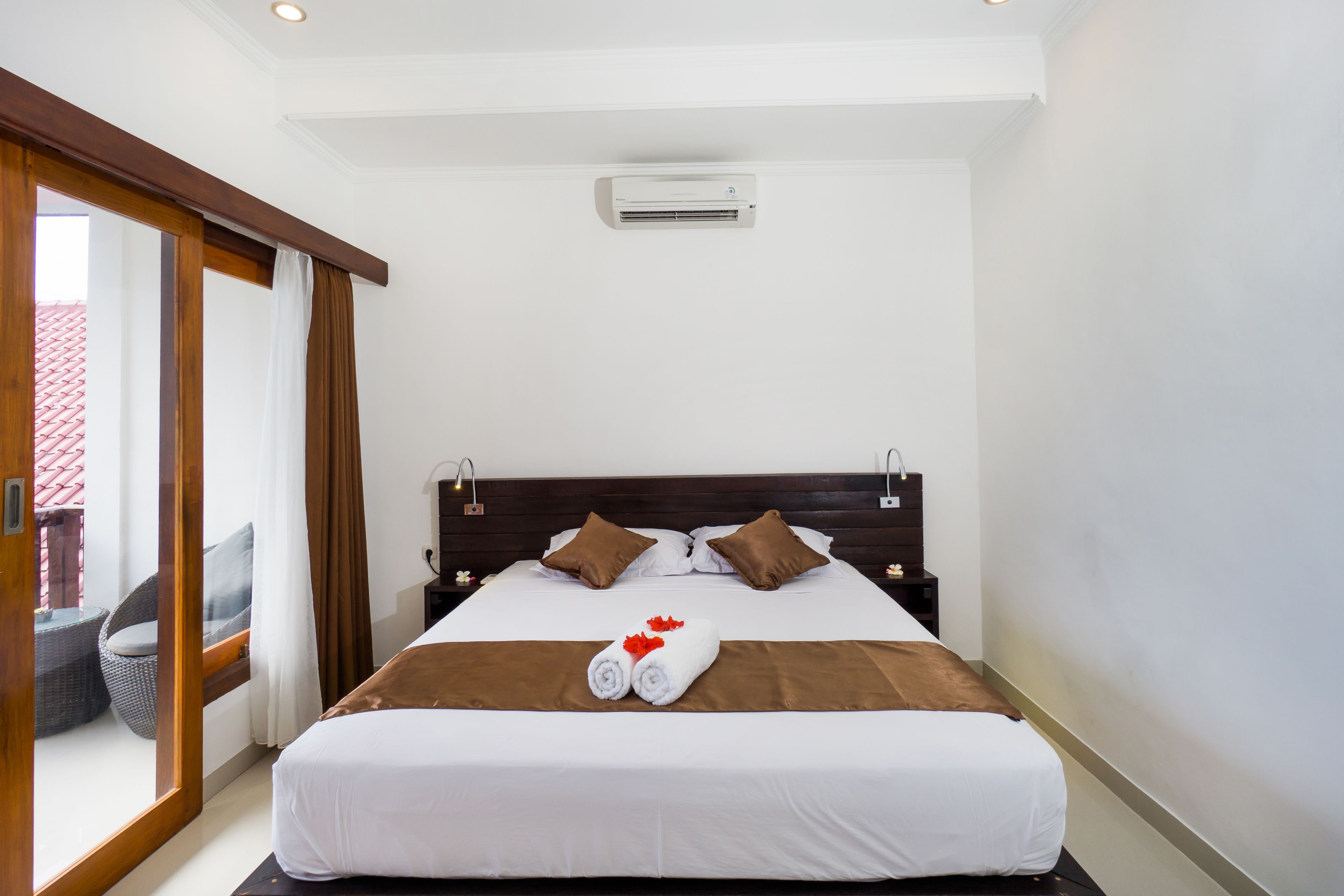 Quarto de hotel com cama, mesa de cabeceira, ar condicionado fixado na parede e porta de vidro deslizante para área externa.