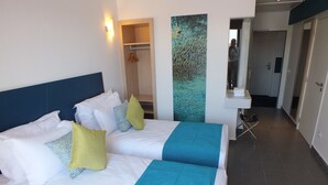 Quarto de hotel com duas camas, um guarda-roupa, um espelho e uma escrivaninha.