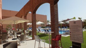 Área de piscina com espreguiçadeiras e guarda-sóis, uma placa com regras e uma construção de tijolos.