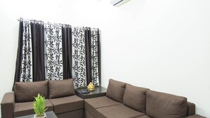 Uma sala moderna com um sofá seccional marrom, uma mesinha lateral com um objeto decorativo e uma janela com cortinas estampadas.