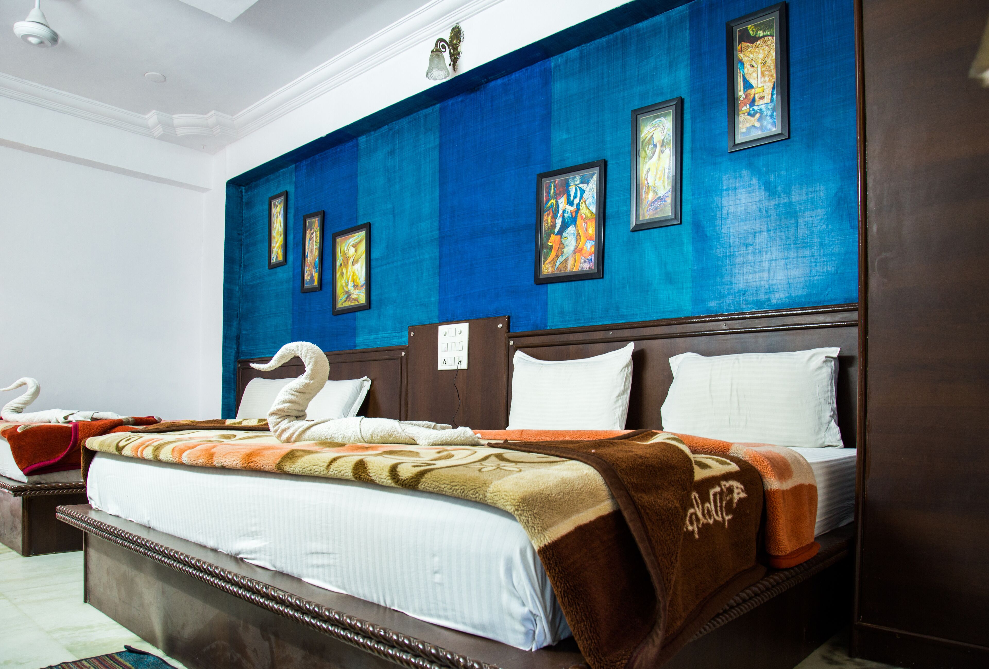 Quarto de hotel com uma cama grande, uma parede de destaque azul e obras de arte emolduradas.