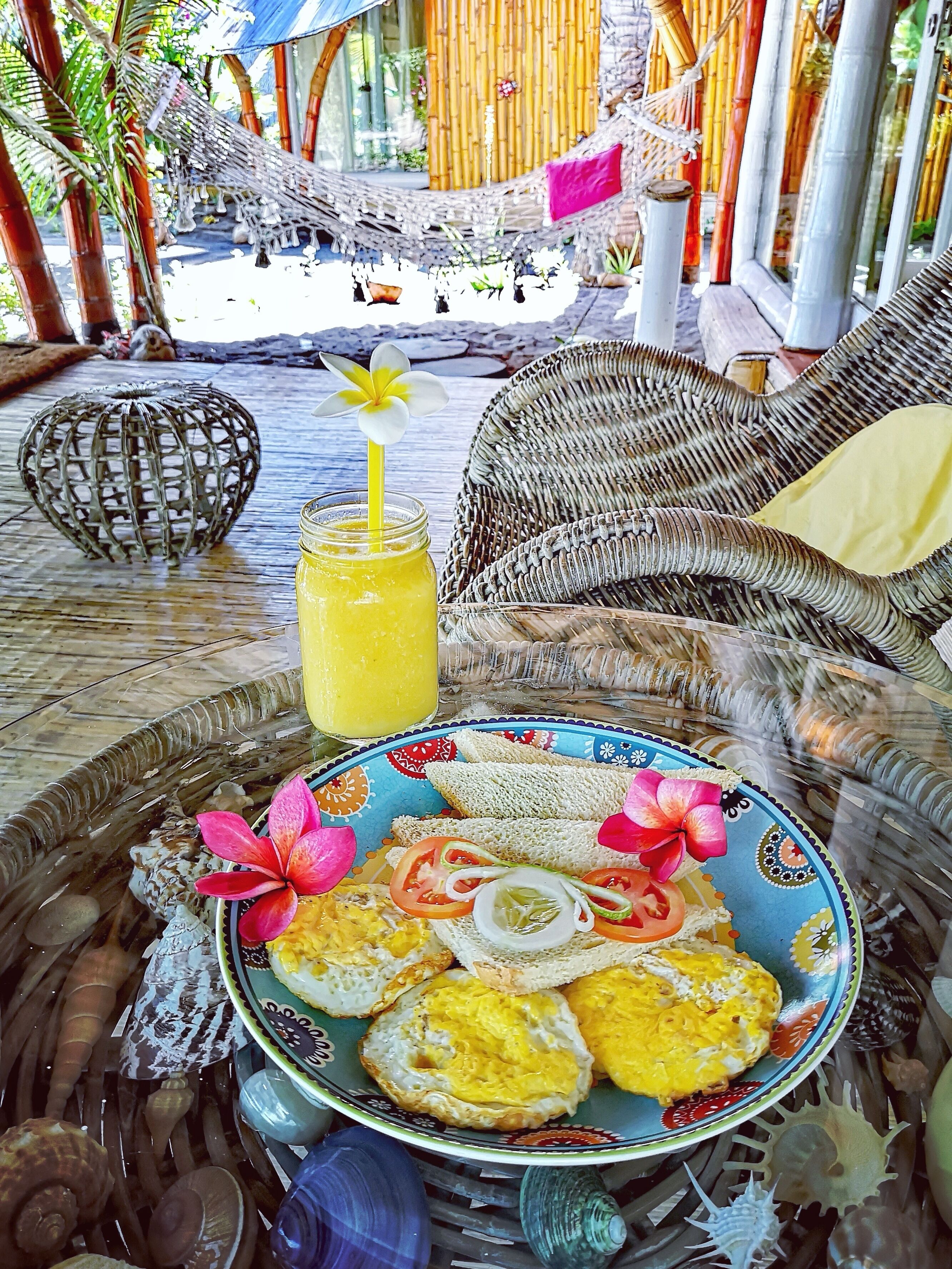 Ambiente tropical com uma cadeira de vime, um prato de comida e uma bebida sobre uma mesa.