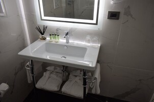 Casa de banho moderna com lavatório branco, espelho e azulejos de mármore. Há duas toalhas penduradas em barras de toalha e um copo de água no lavatório.