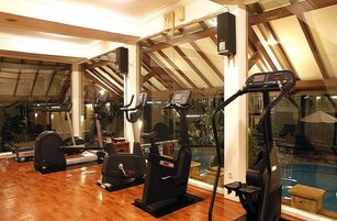 Academia com equipamentos de ginástica, janelas amplas e vista para uma piscina.