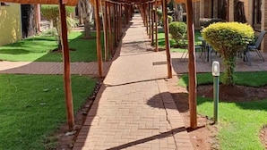 Uma galeria coberta com caminho de tijolos, postes de madeira e telhado de palha.