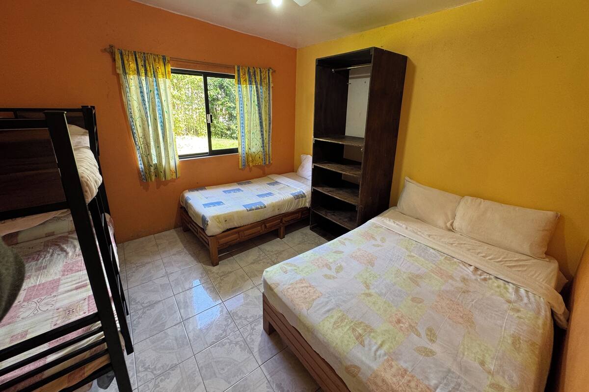 Um quarto em dormitório com duas camas, um guarda-roupa, uma janela com cortinas e um ventilador de teto.