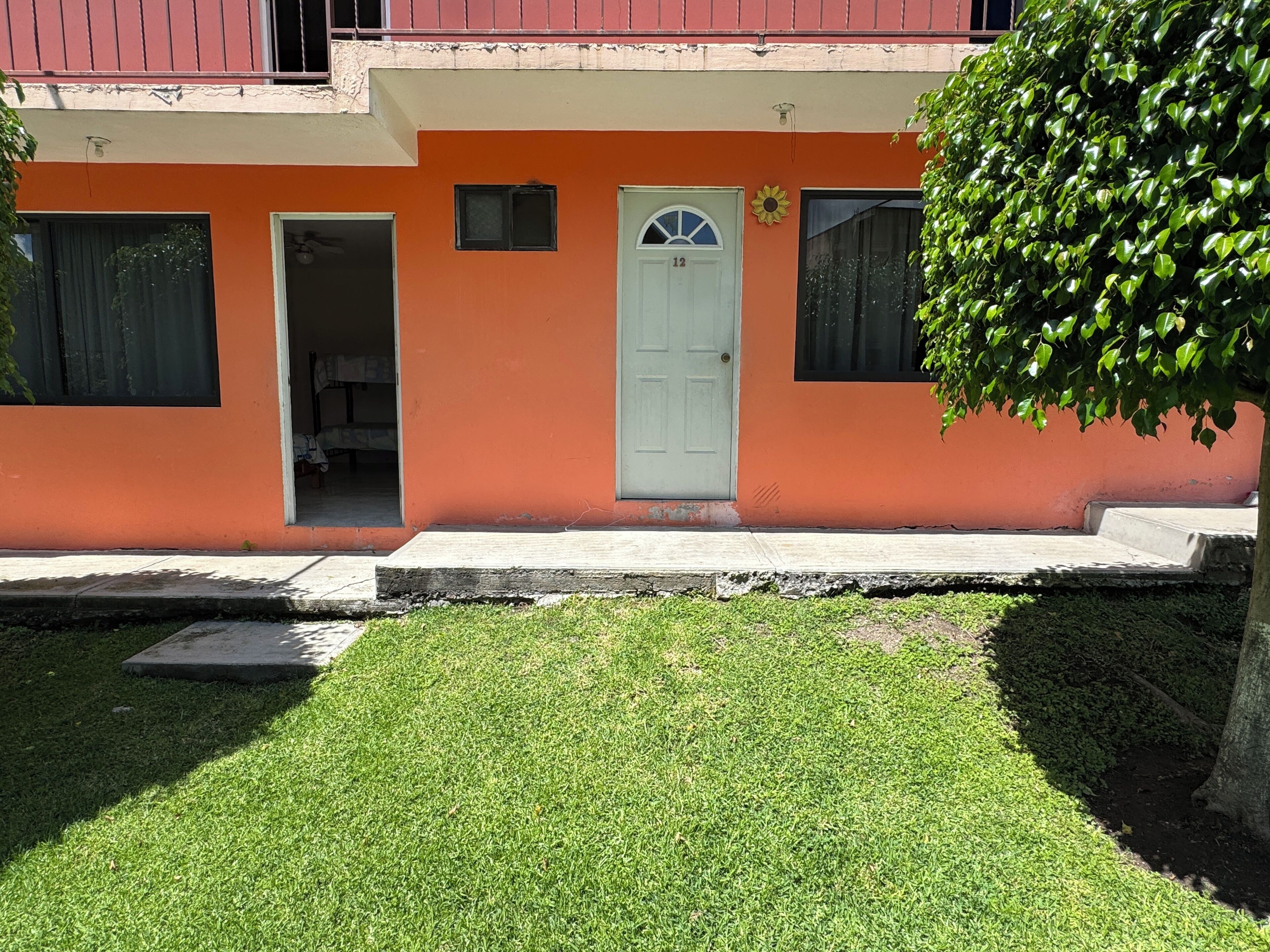 Um edifício de dois andares com fachada vermelha, porta branca e uma pequena janela com decoração solar.