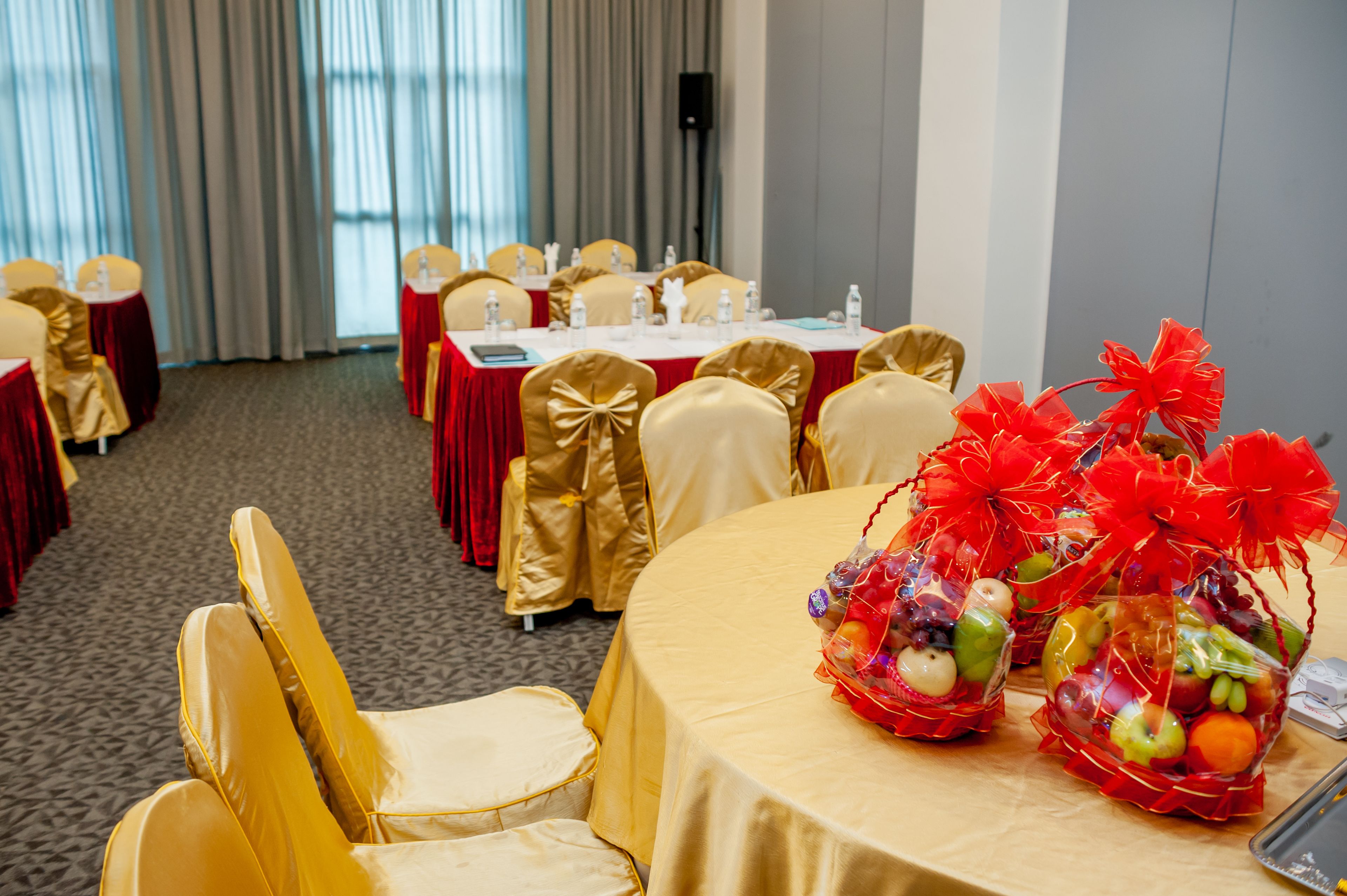 Sala de conferências com mesas redondas, cadeiras e um buffet com cestas de fruta.