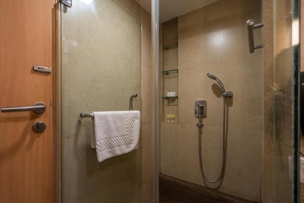 Casa de banho com porta de vidro, um porta-toalhas com toalha branca, chuveiro com chuveiro manual e cabine de duche em vidro.