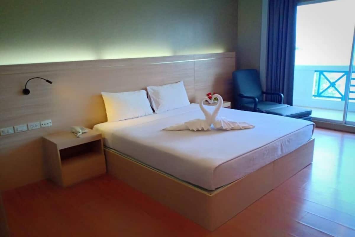 Quarto de hotel com uma cama grande, mesa de cabeceira, uma cadeira e vista para o exterior.