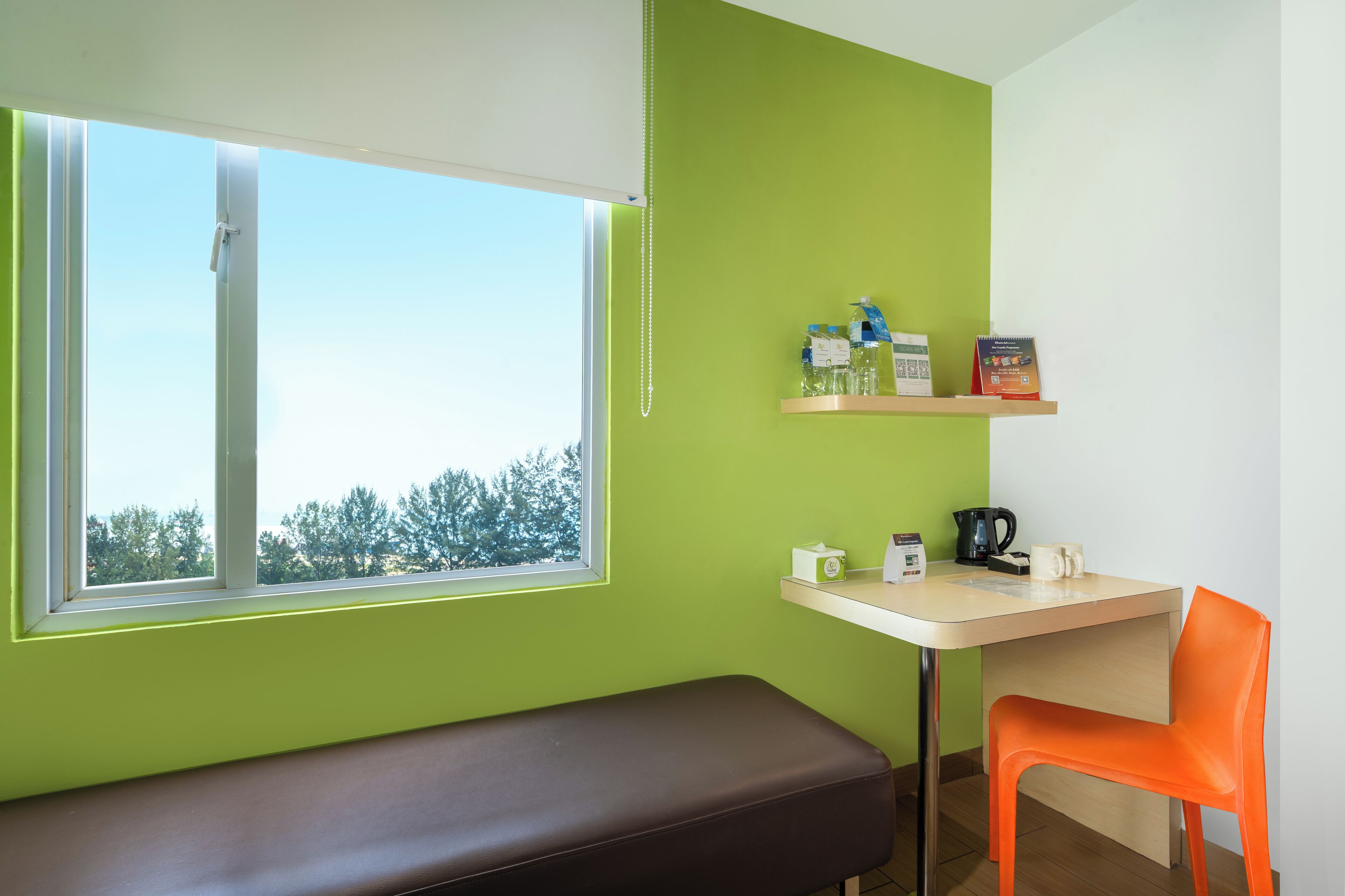 Um quarto com uma janela grande, um banco, uma mesa com uma cadeira e estantes com objetos.