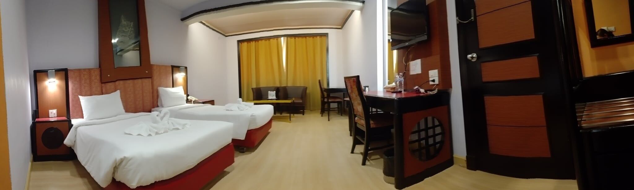 Quarto de hotel com duas camas, uma escrivaninha, uma cadeira, uma televisão e uma janela com cortinas.