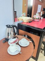 Quarto de hotel com uma mesa de madeira posta para chá, chaleira e um objeto decorativo pequeno.