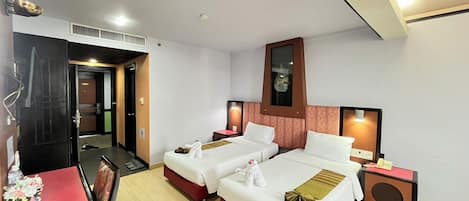 Quarto de hotel com duas camas, uma escrivaninha e uma cadeira. Há um espelho sobre as camas e uma pequena mesa com toalha de mesa vermelha.
