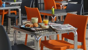 Uma mesa de café da manhã com croissants, uma tigela de iogurte, um copo de suco de laranja e um jornal.