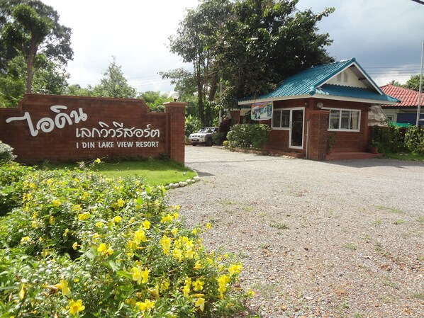 Placa de identificação do I Din Lake View Resort, com uma entrada de cascalho e um pequeno edifício com telhado azul.