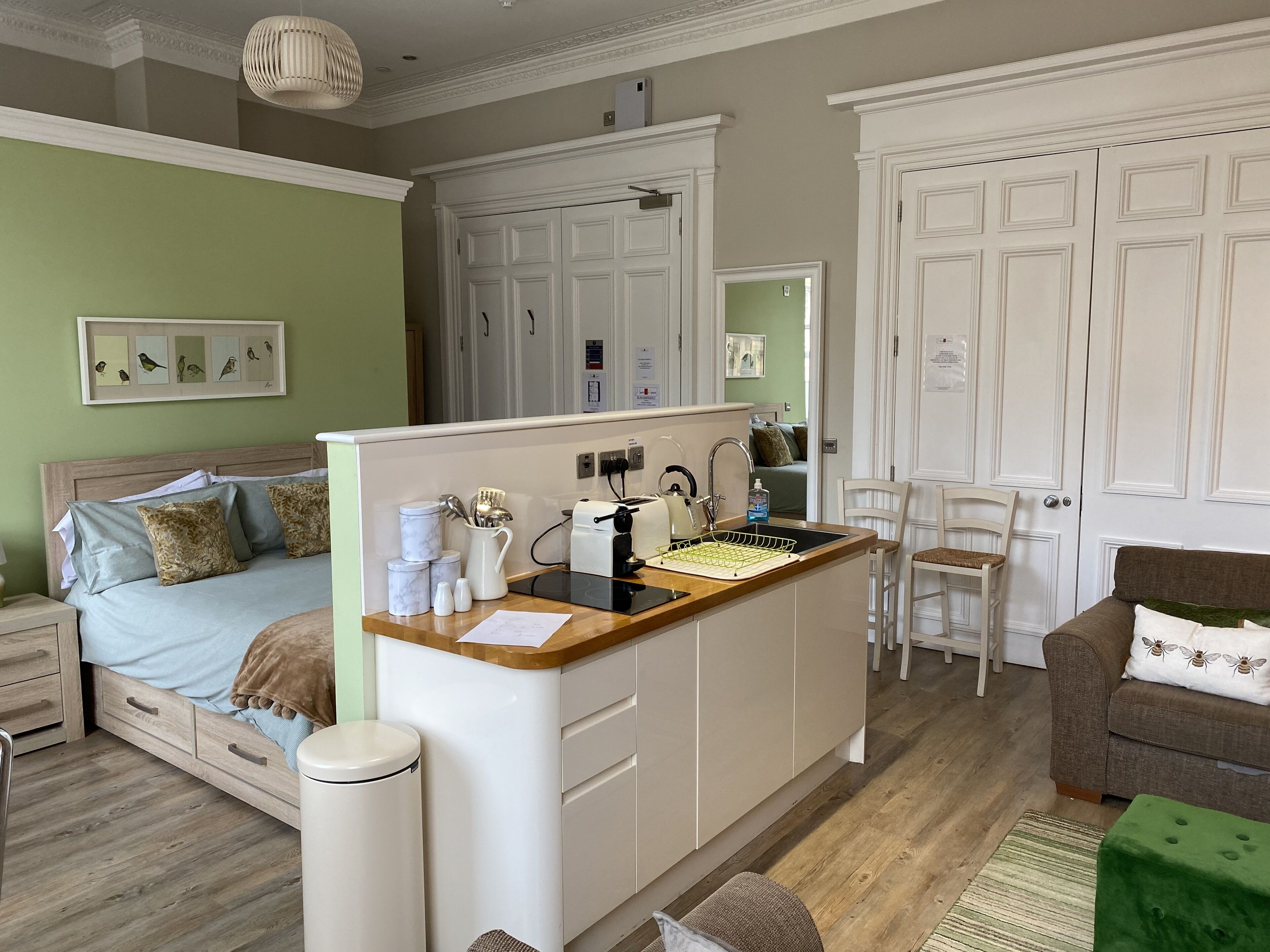 Quarto moderno com cama, mesas de cabeceira, pequeno espaço de cozinha e um sofá verde.