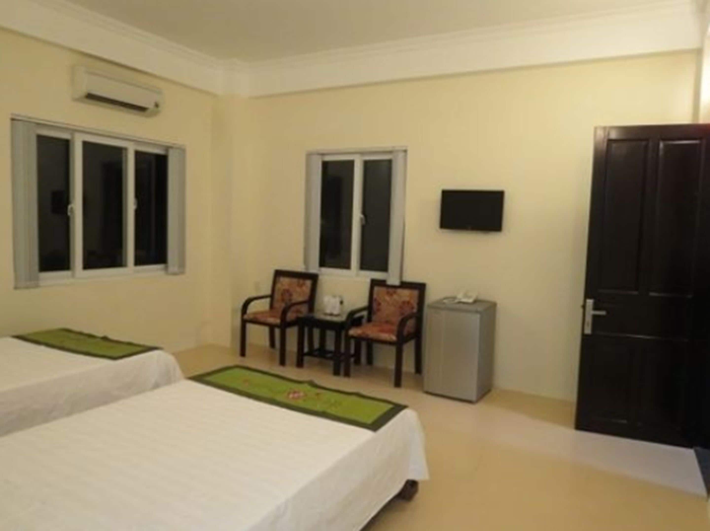 Quarto de hotel com duas camas, uma escrivaninha, uma cadeira, uma televisão e uma porta.