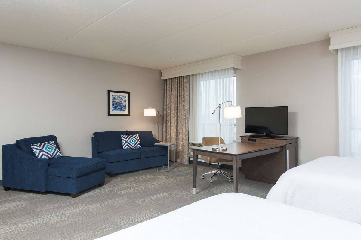 Quarto de hotel com cama, escrivaninha, poltrona, sofá e televisão.