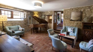 Uma sala de estar acolhedora com um piano de cauda, duas poltronas azul claro, uma mesa de centro de madeira e uma parede de pedra.