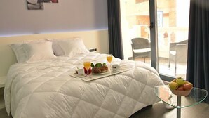 Quarto de hotel com cama, bandeja de café da manhã e mesa de vidro com frutas.