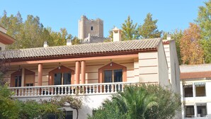Um edifício com varanda, uma torre ao fundo e árvores ao redor.