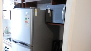Cozinha compacta com geladeira, micro-ondas e um pequeno balcão com cesta.