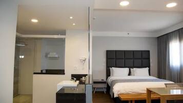 Quarto de hotel moderno com uma cama grande, uma mesinha de cabeceira, uma escrivaninha pequena e um espelho.