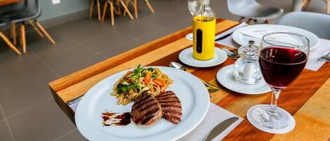 Uma mesa de jantar com uma refeição de carne grelhada, massa e um copo de vinho tinto.