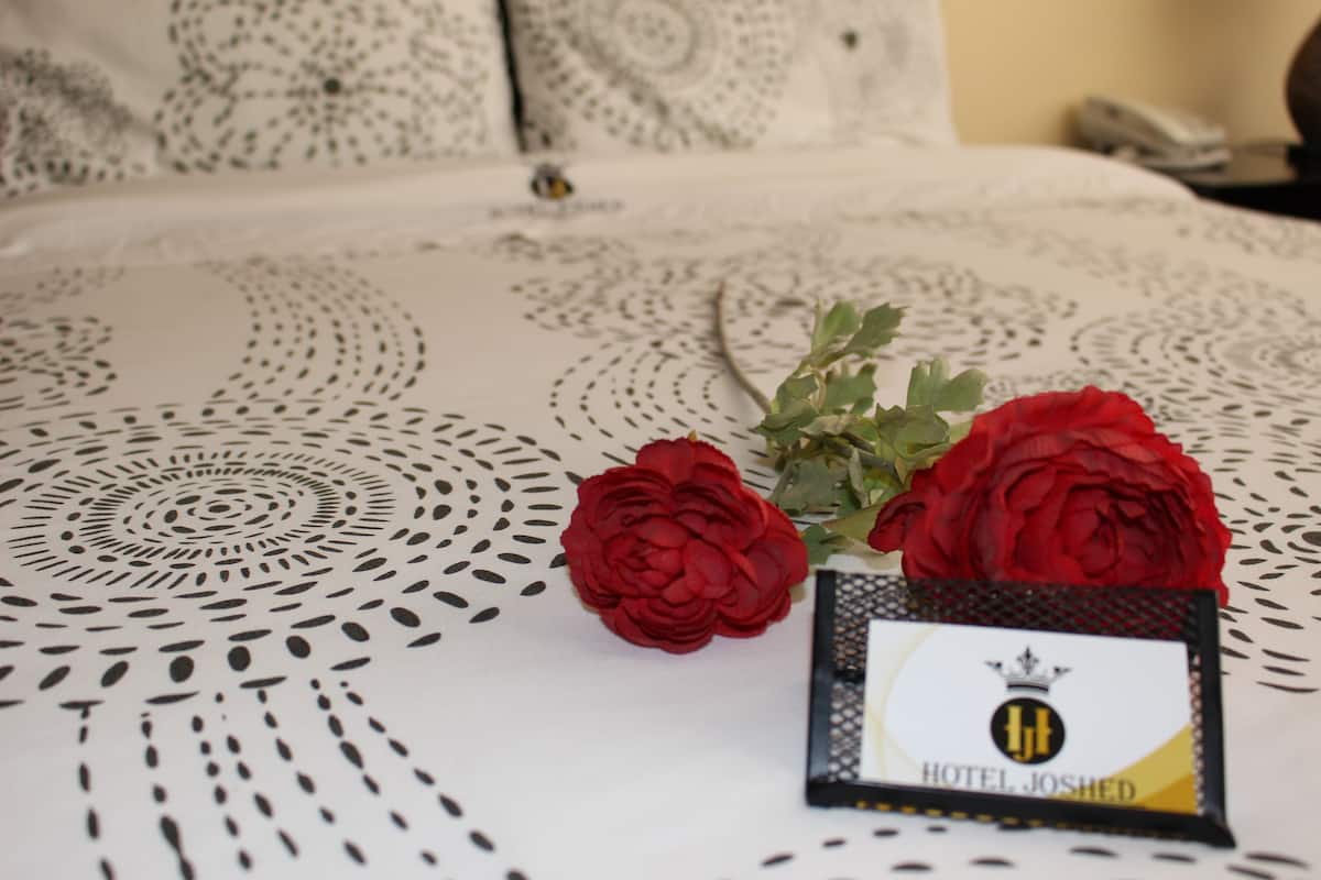 Uma cama com um edredom estampado em branco e preto, uma rosa vermelha e uma placa do Hotel Joshed.