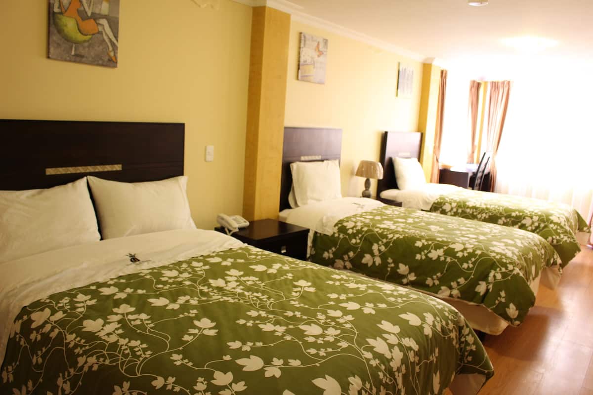 Quarto de hotel com duas camas de solteiro, uma mesinha de cabeceira com abajur e um telefone.