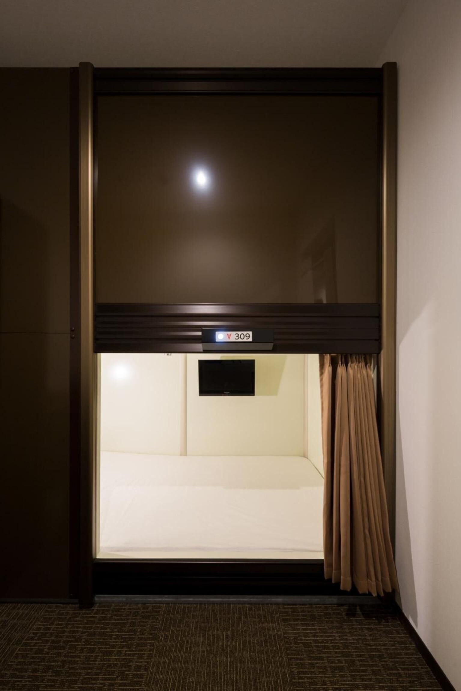 Quarto de hotel com uma cama de solteiro, uma televisão pequena e uma cortina.