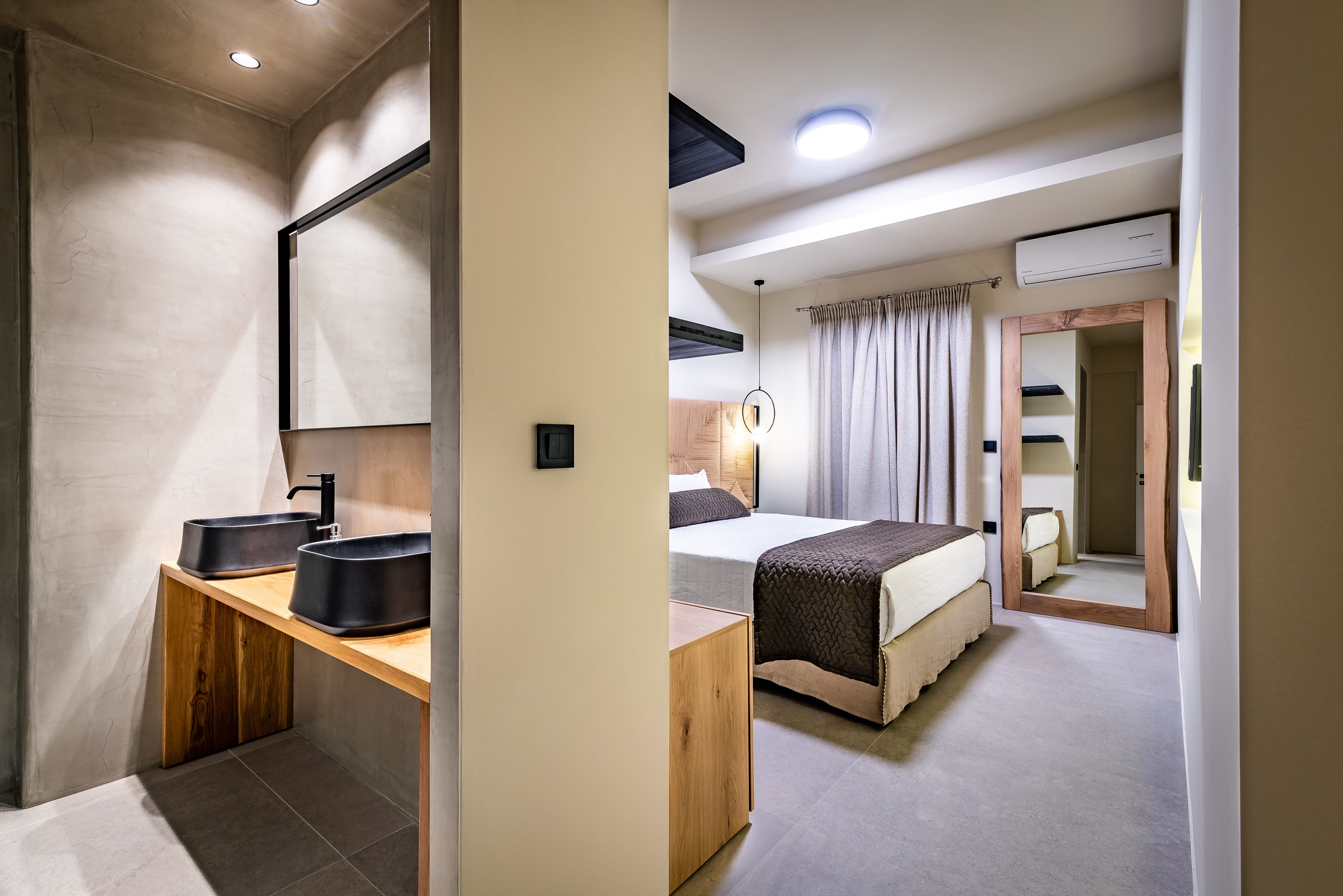 Quarto de hotel moderno com toucador de madeira, uma cama com cabeceira, mesa de cabeceira e um espelho grande.
