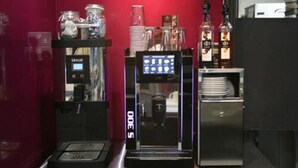 Máquina de café com visor digital, balança e recipiente de vidro sobre uma bancada.