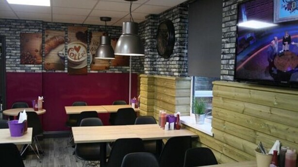 Interior de restaurante com paredes de tijolo, mesas de madeira e cadeiras pretas.