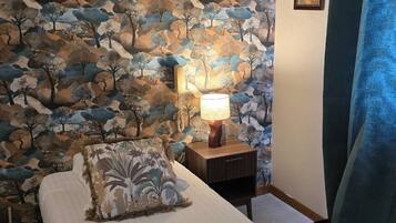 Quarto de hotel com uma cama, uma mesa de cabeceira com abajur, um quadro na parede e uma cortina azul.