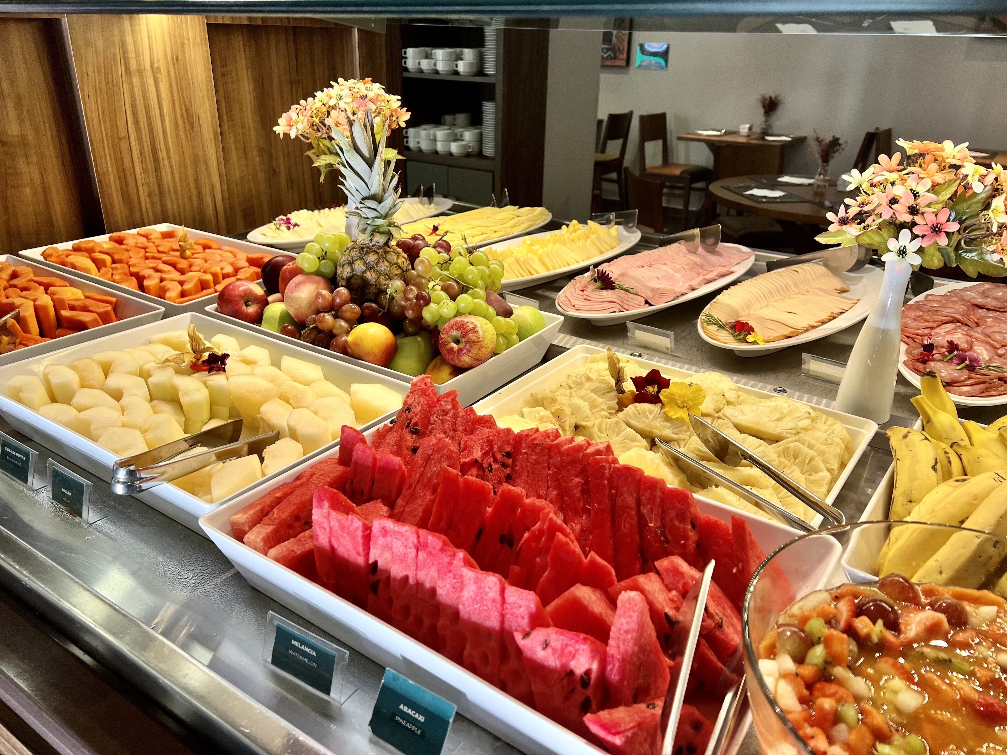 Um buffet com diversas frutas e legumes, incluindo melancia, abacaxi e uvas.