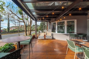 Um pátio externo com piso de madeira, cadeiras verdes com almofadas e uma mesa.