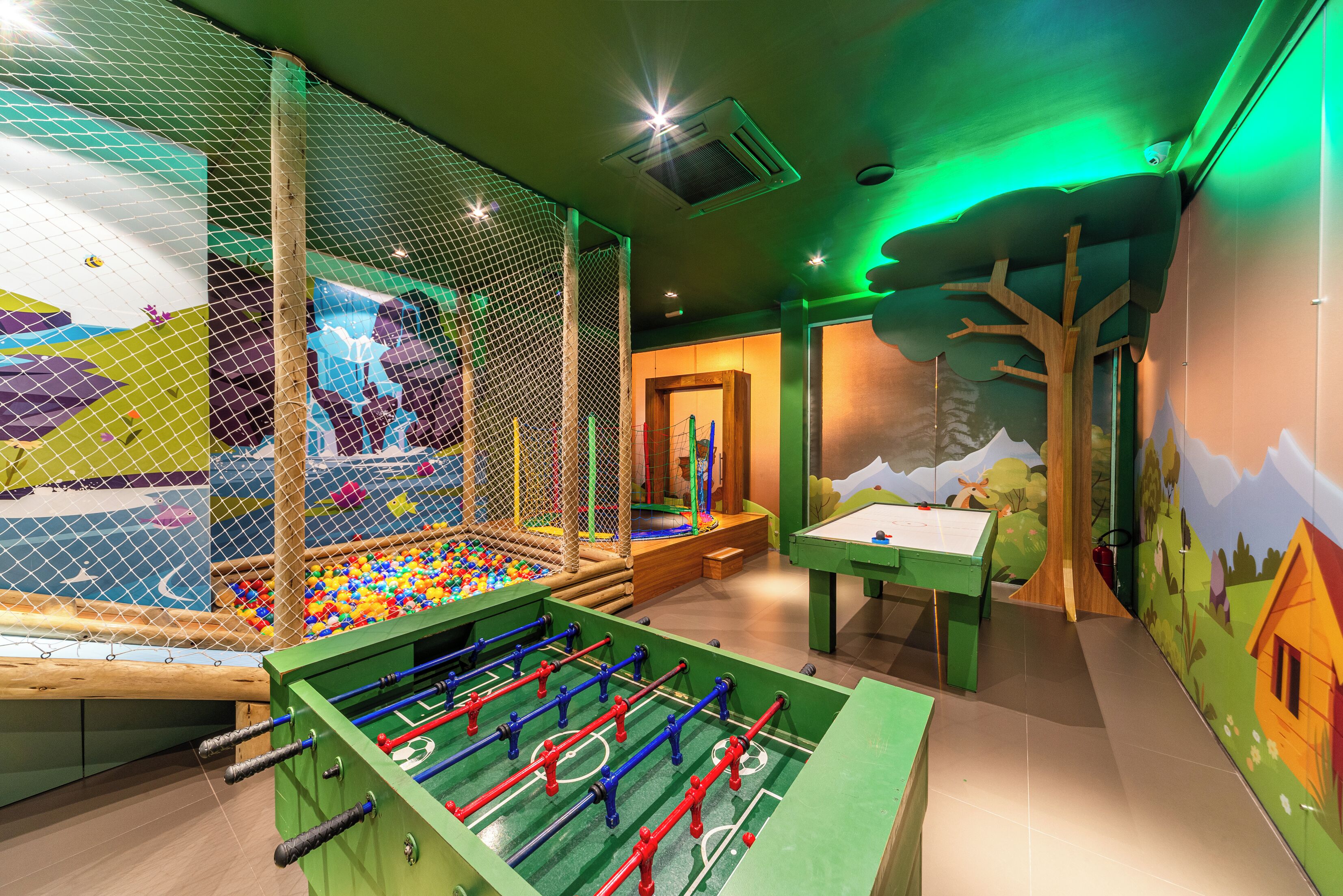 Espaço infantil com mesa de futebol de mesa, piscina de bolinhas e rede de escalada.