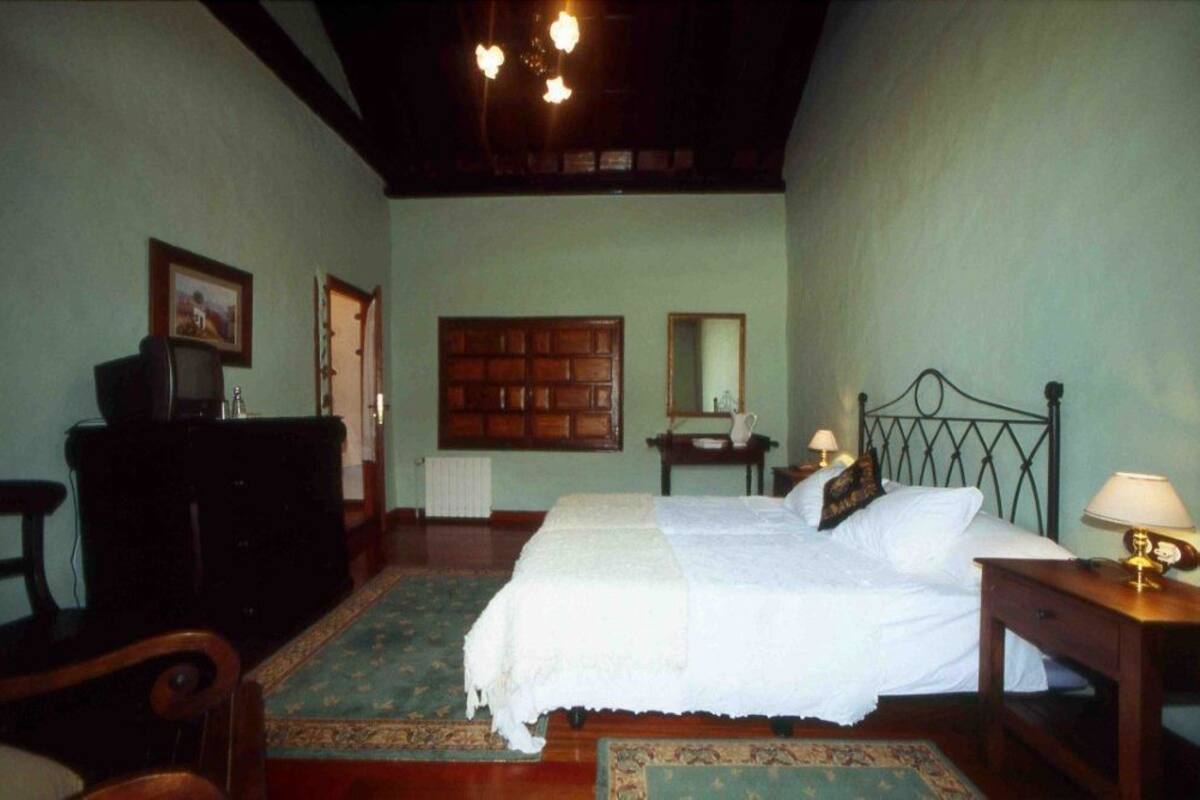 Um quarto com uma cama grande, cômoda de madeira, escrivaninha e uma cadeira.