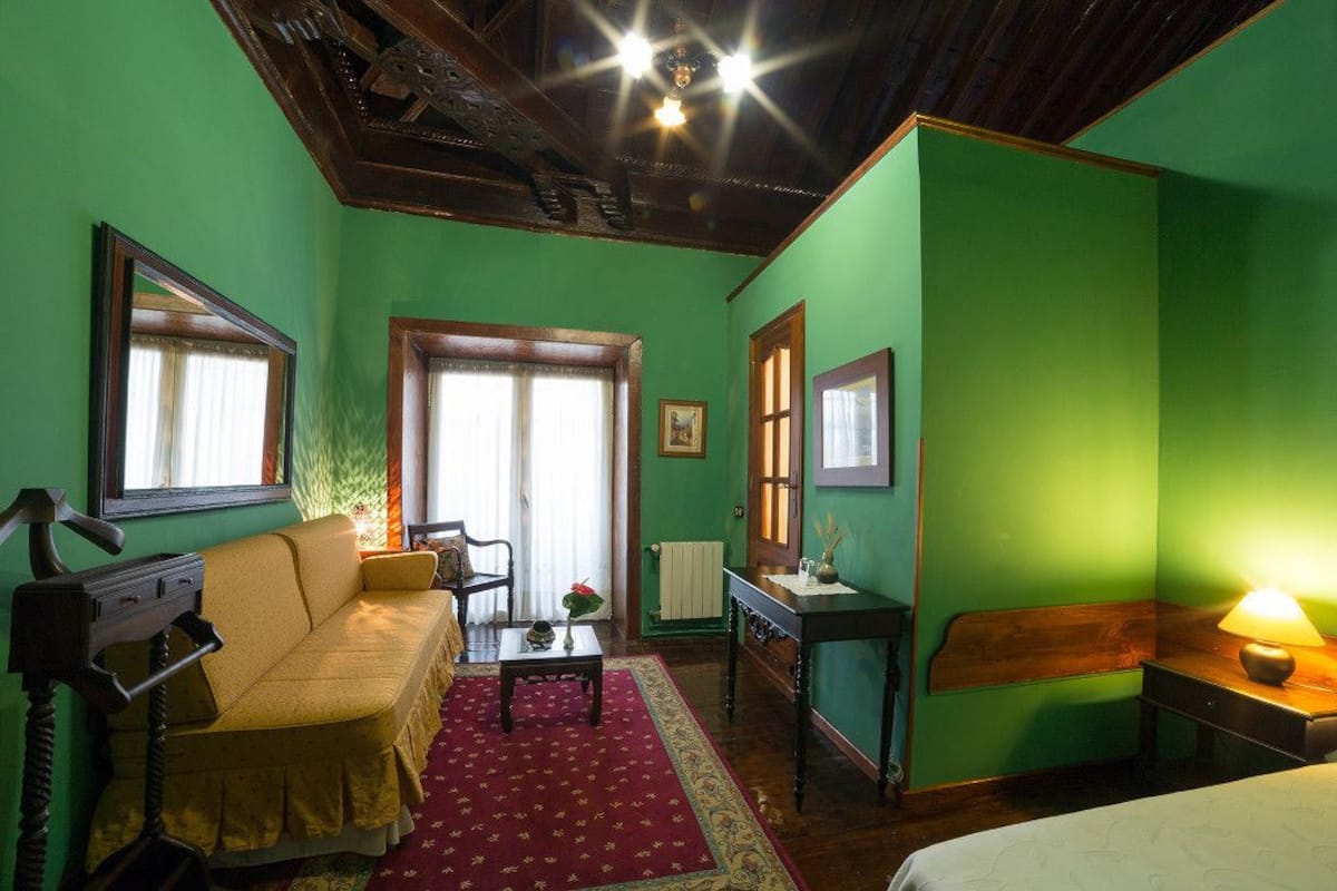 Um quarto com parede verde, teto de madeira, um sofá, uma mesa, um abajur e uma cama.